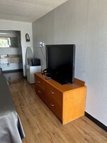 Quarto de hotel com cômoda de madeira, televisão de tela plana, micro-ondas, mini-geladeira, pia e espelho.