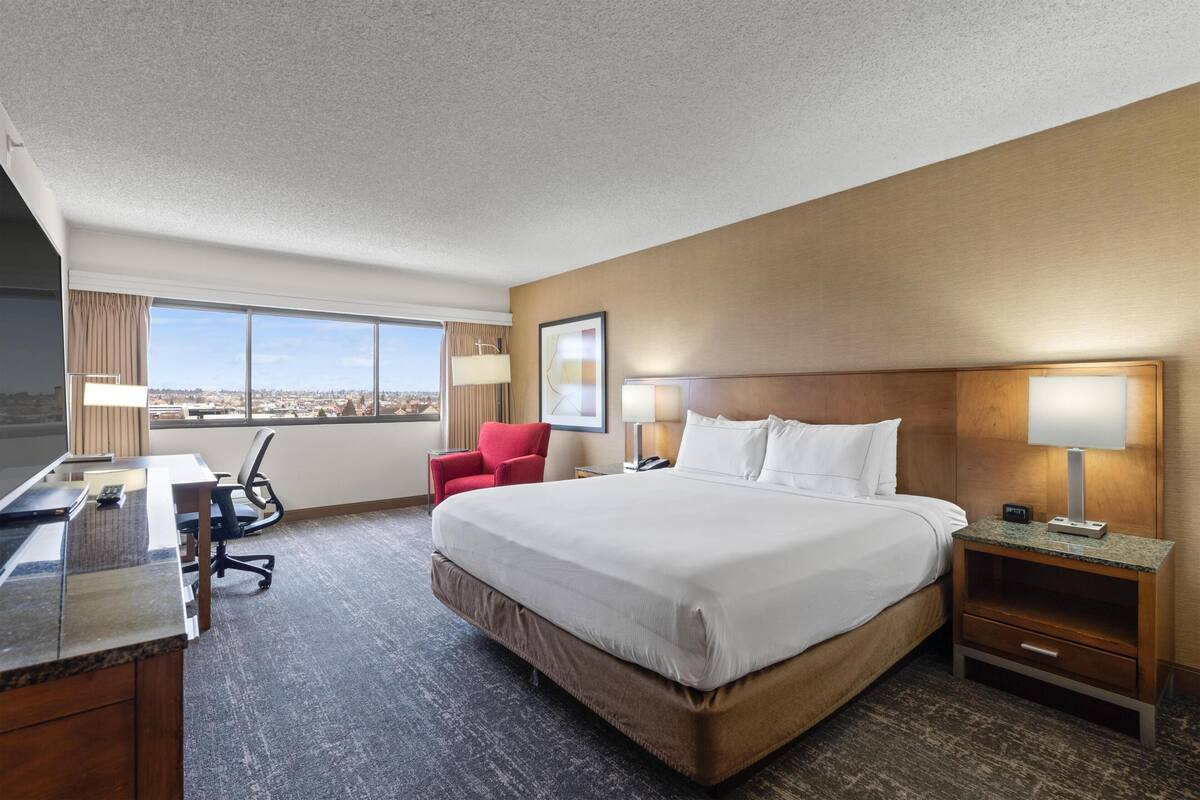 Quarto de hotel com uma cama grande, uma escrivaninha, uma cadeira, uma mesa de cabeceira e vista para a cidade.