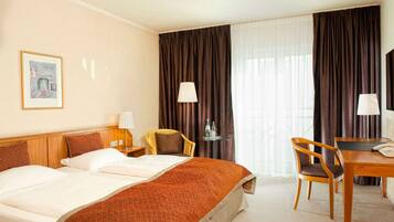 Quarto de hotel com uma cama, duas cadeiras, uma escrivaninha, um abajur e um quadro na parede.