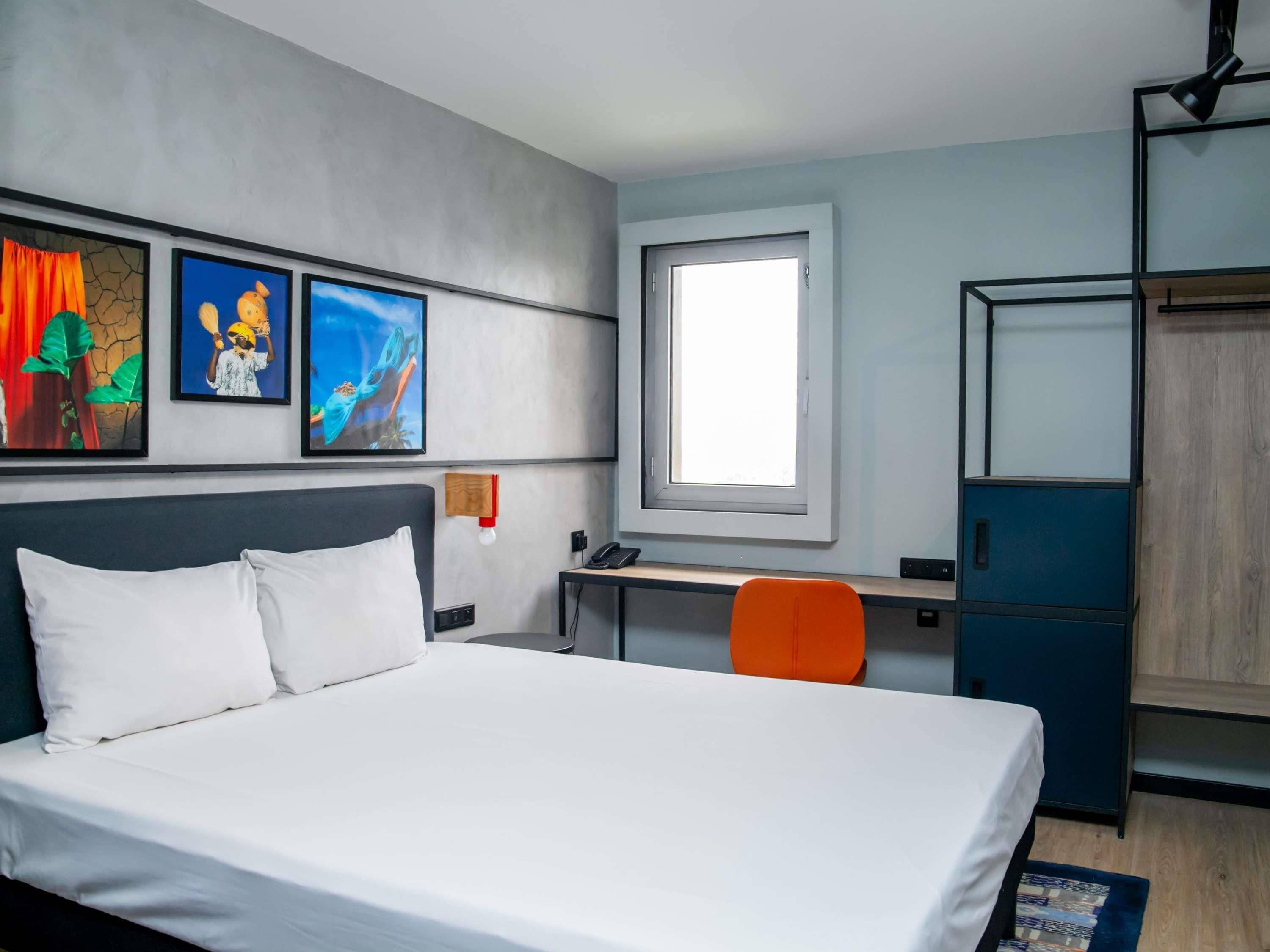 Quarto de hotel com cama, escrivaninha, cadeira e obra de arte na parede.