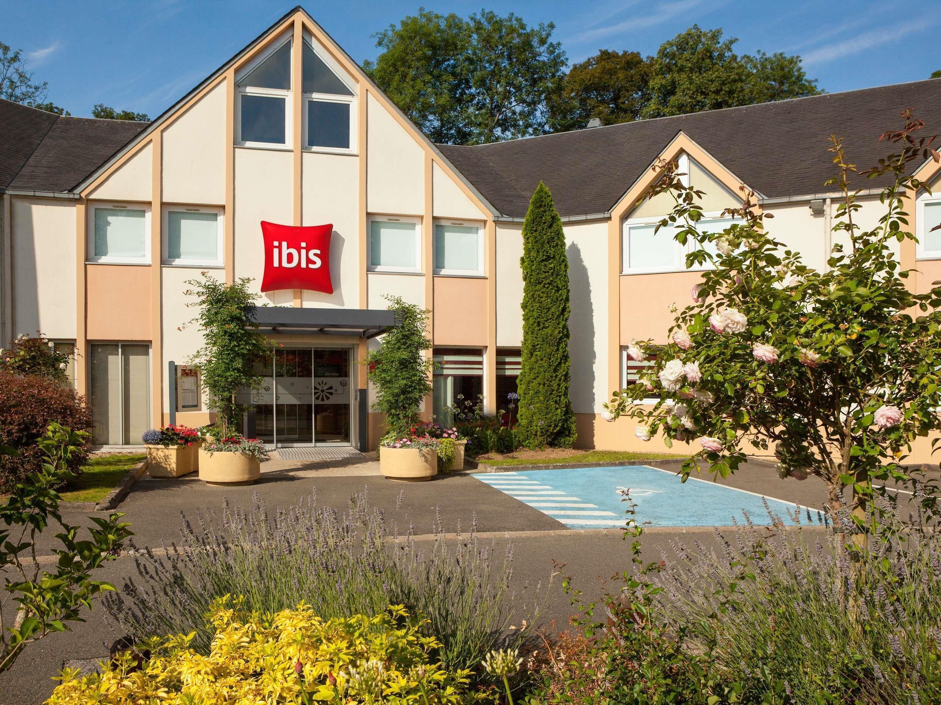 Um hotel com um grande letreiro vermelho da Ibis, um hall com paisagismo e uma piscina.