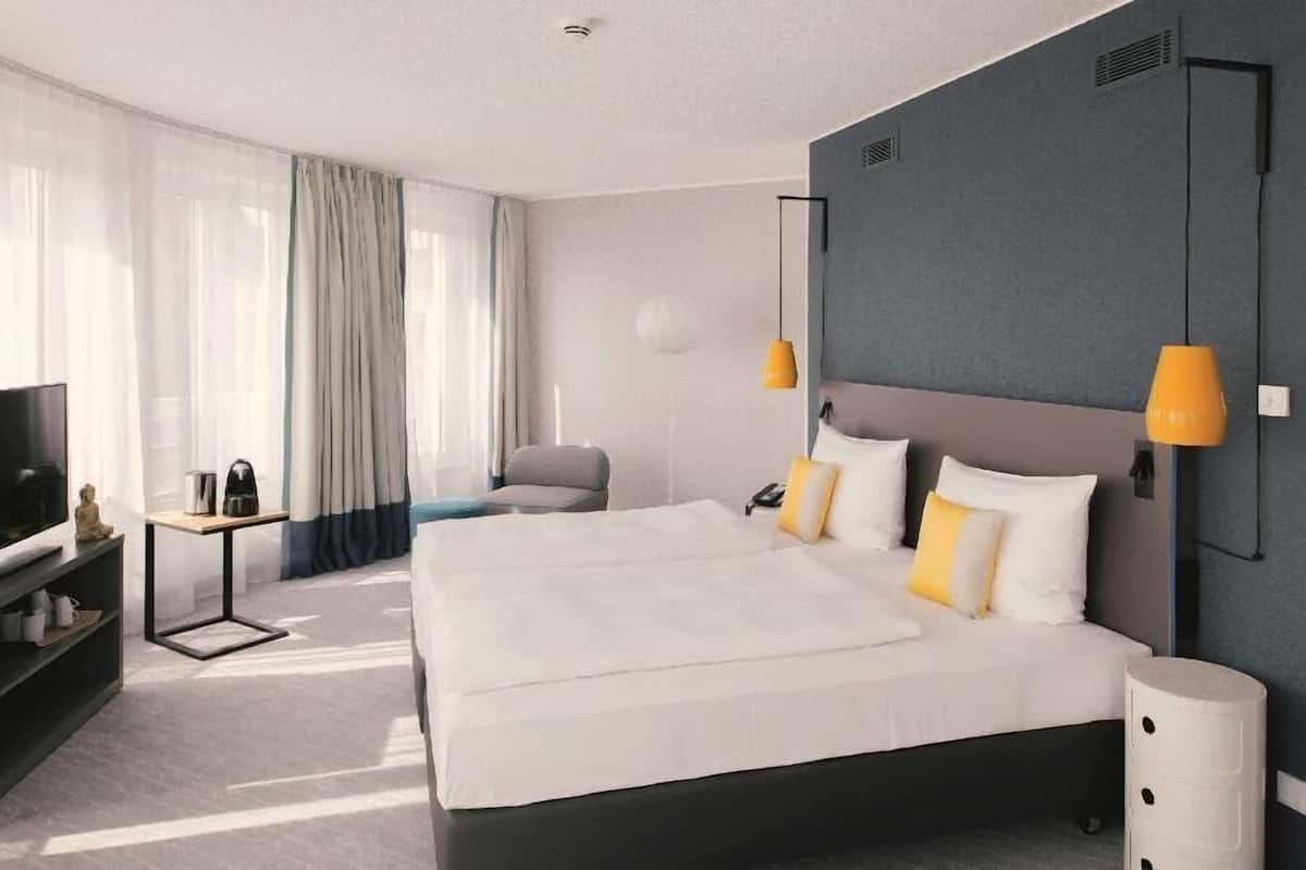 Quarto de hotel com uma cama grande, uma escrivaninha, uma cadeira e uma televisão.