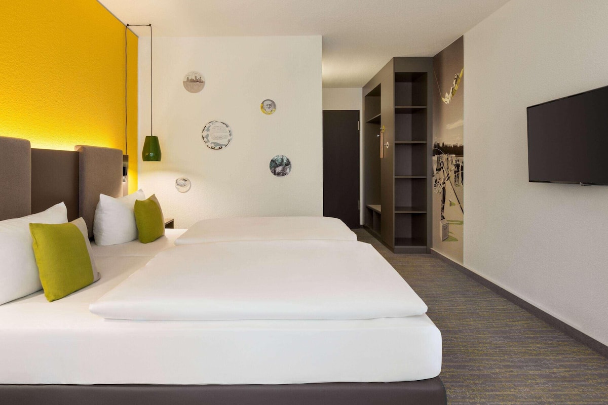 Quarto de hotel com uma cama grande, uma televisão na parede e um guarda-roupa com espelho.