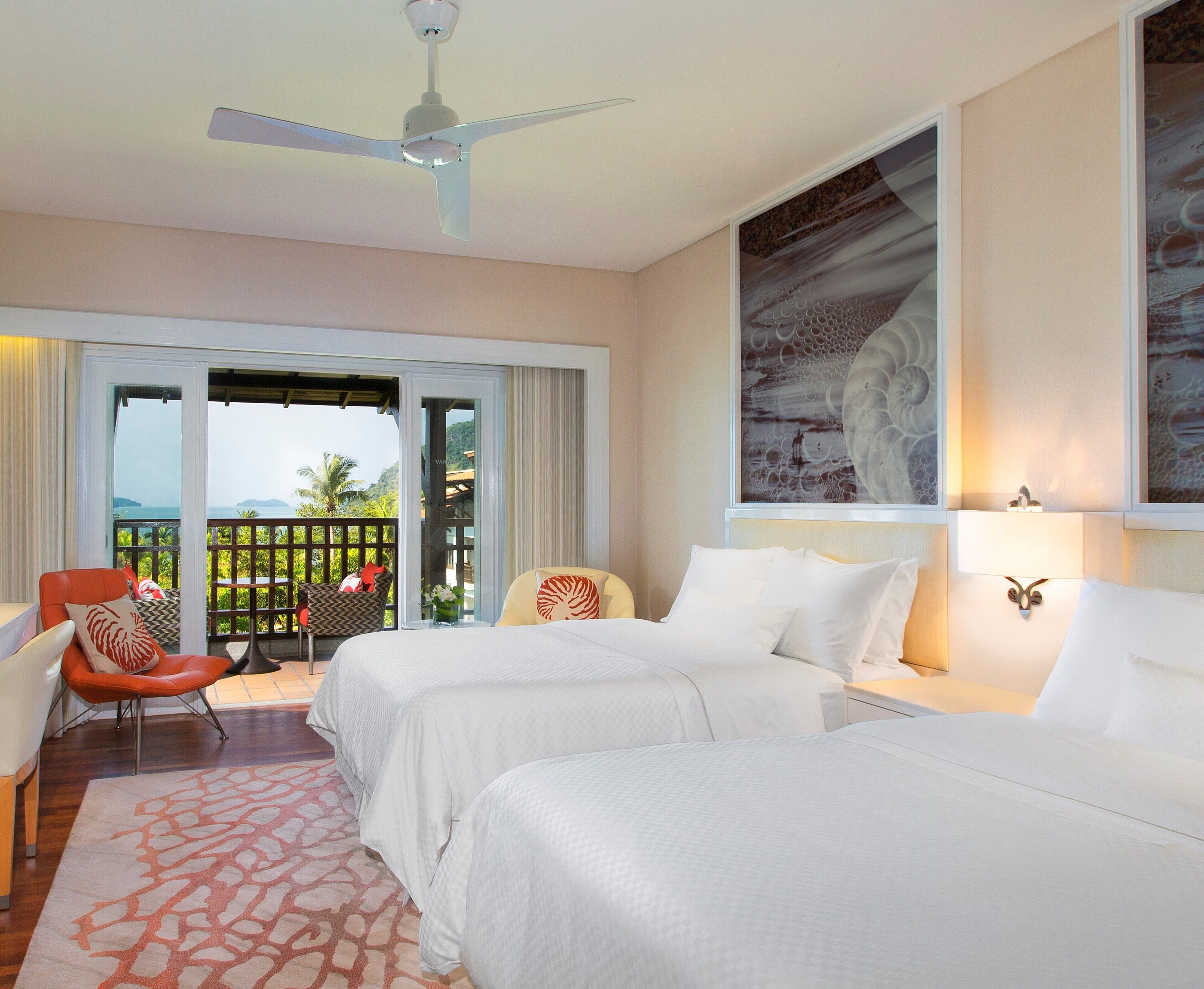 Quarto de hotel com duas camas, ventoinha no teto, varanda com vista e um quadro na parede.