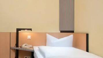 Quarto de hotel com cama, mesa de cabeceira, abajur e luminária na parede.