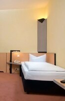 Quarto de hotel com cama, mesa de cabeceira, abajur e luminária na parede.
