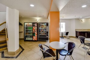 Um hall de hotel com escadas, máquinas de venda automática e uma área de estar com mesas e cadeiras.