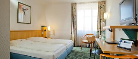 Quarto de hotel com duas camas, uma mesa com um laptop, uma cadeira, uma TV e uma janela com cortinas.