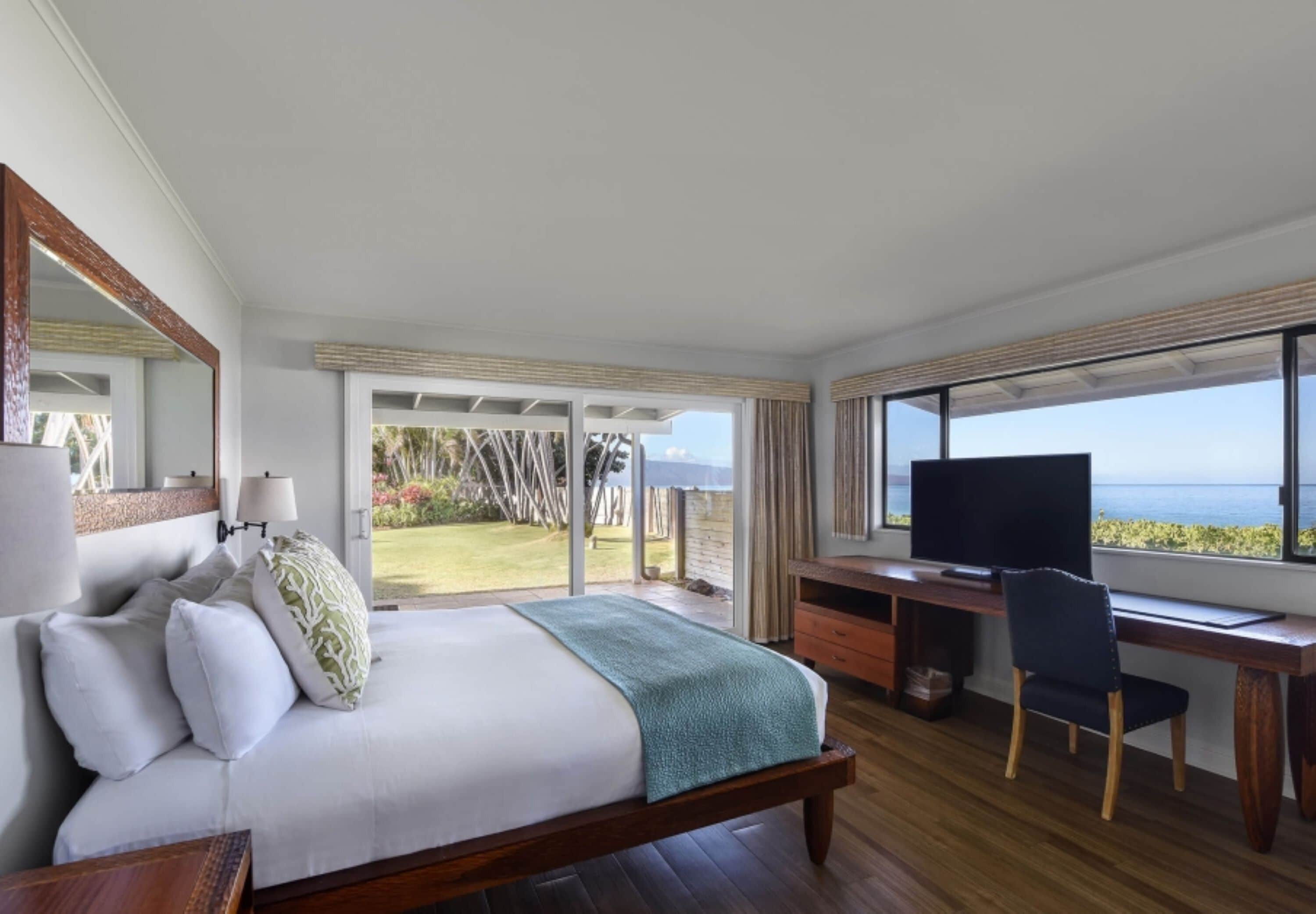 Quarto com cama, escrivaninha, televisão e vista para o mar.