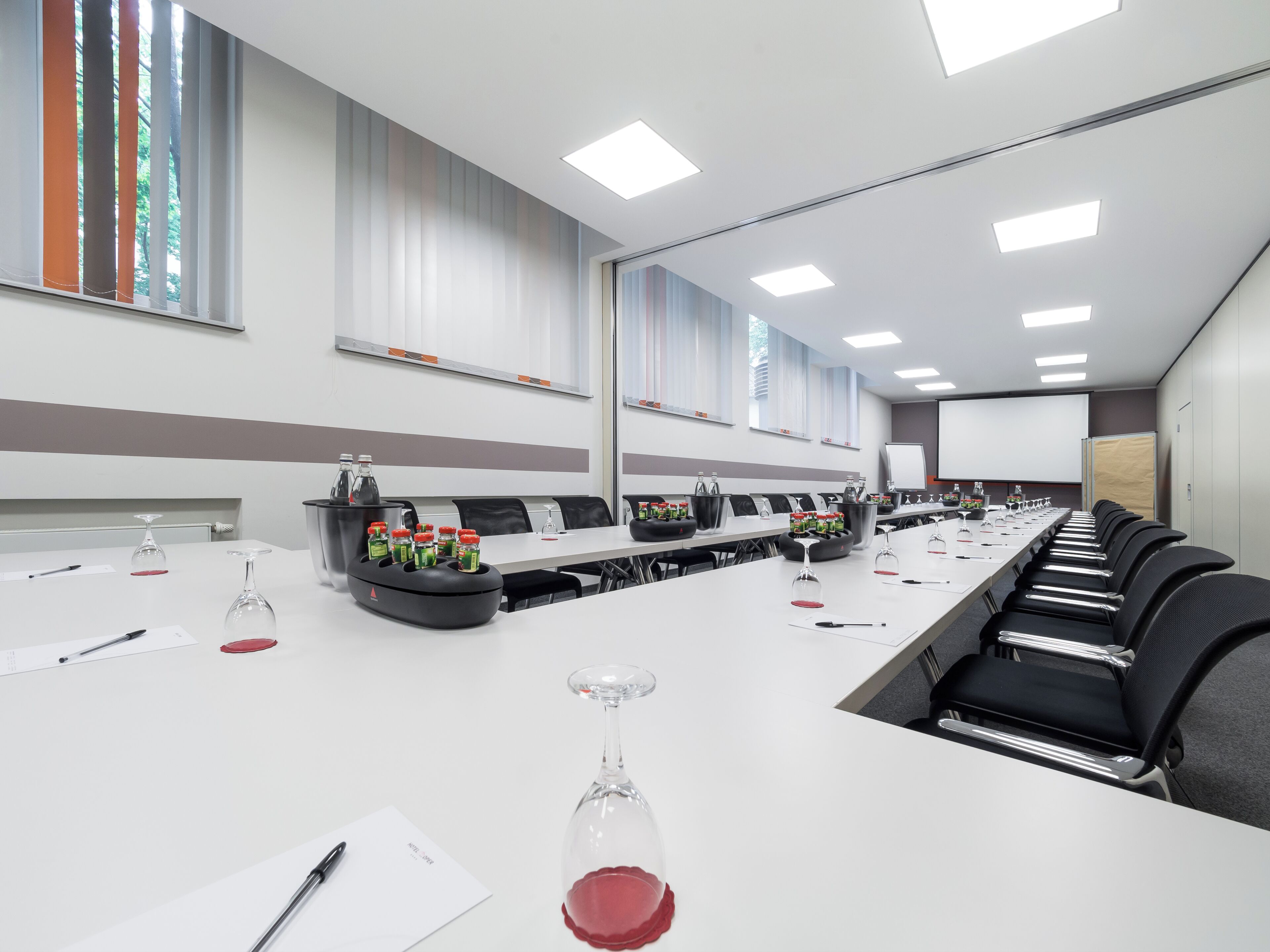 Sala de conferência com uma mesa comprida, cadeiras e tela de projeção.