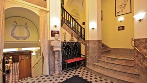 Uma escadaria imponente com piso xadrez, um banco vermelho e um pilar de mármore.