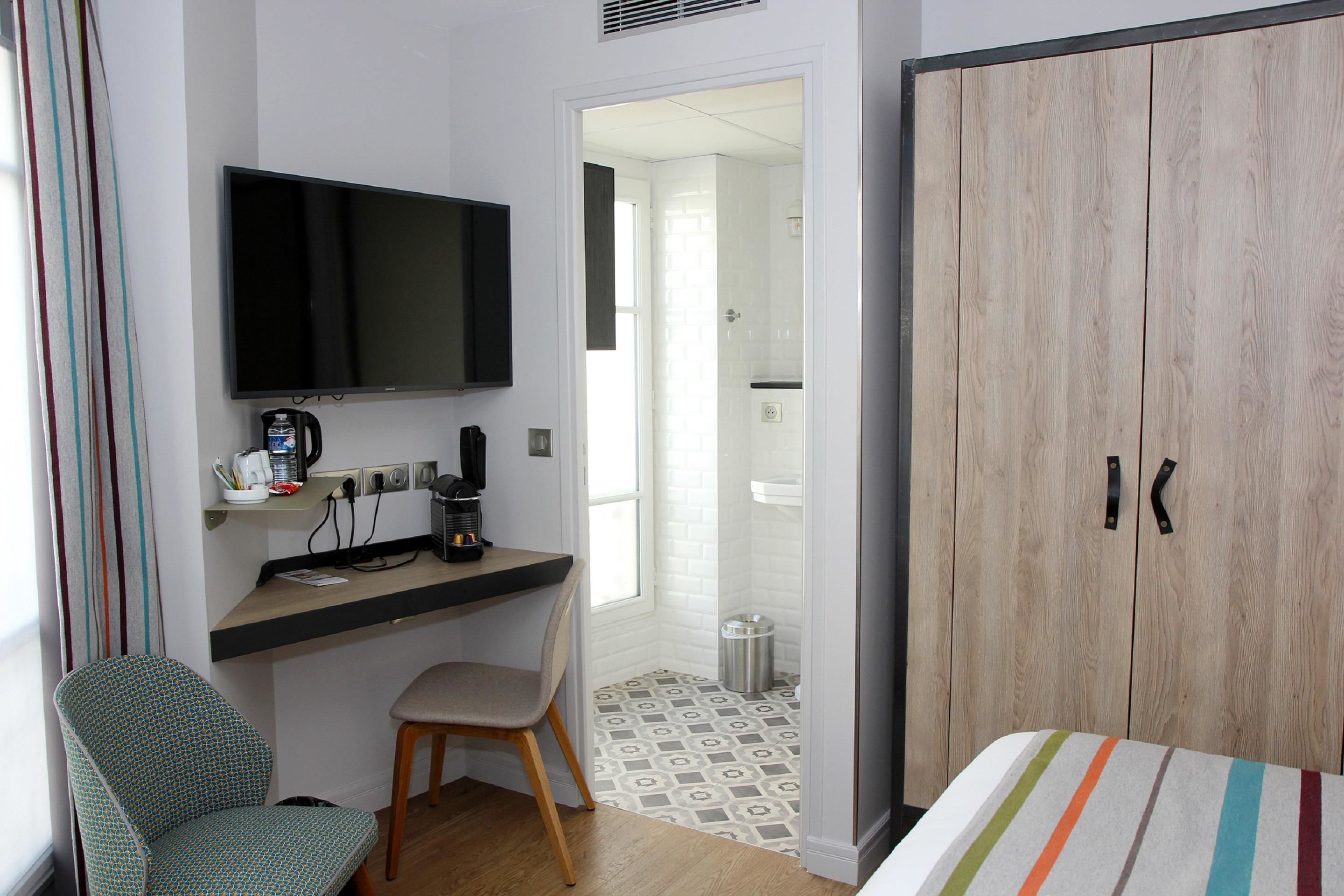 Quarto compacto com uma cama, escrivaninha com cadeira, televisão e guarda-roupa.