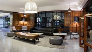 Um hall amplo com um sofá de couro, pufes e uma mesa de centro. Há luminárias pendentes e uma janela grande com vista.