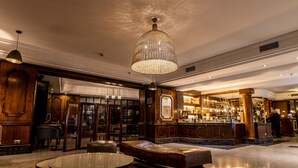 Um hall amplo com um lustre grande e ornamentado, área de bar e assentos confortáveis.