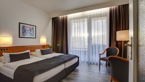 Quarto de hotel com uma cama grande, uma cadeira e uma janela com cortinas.