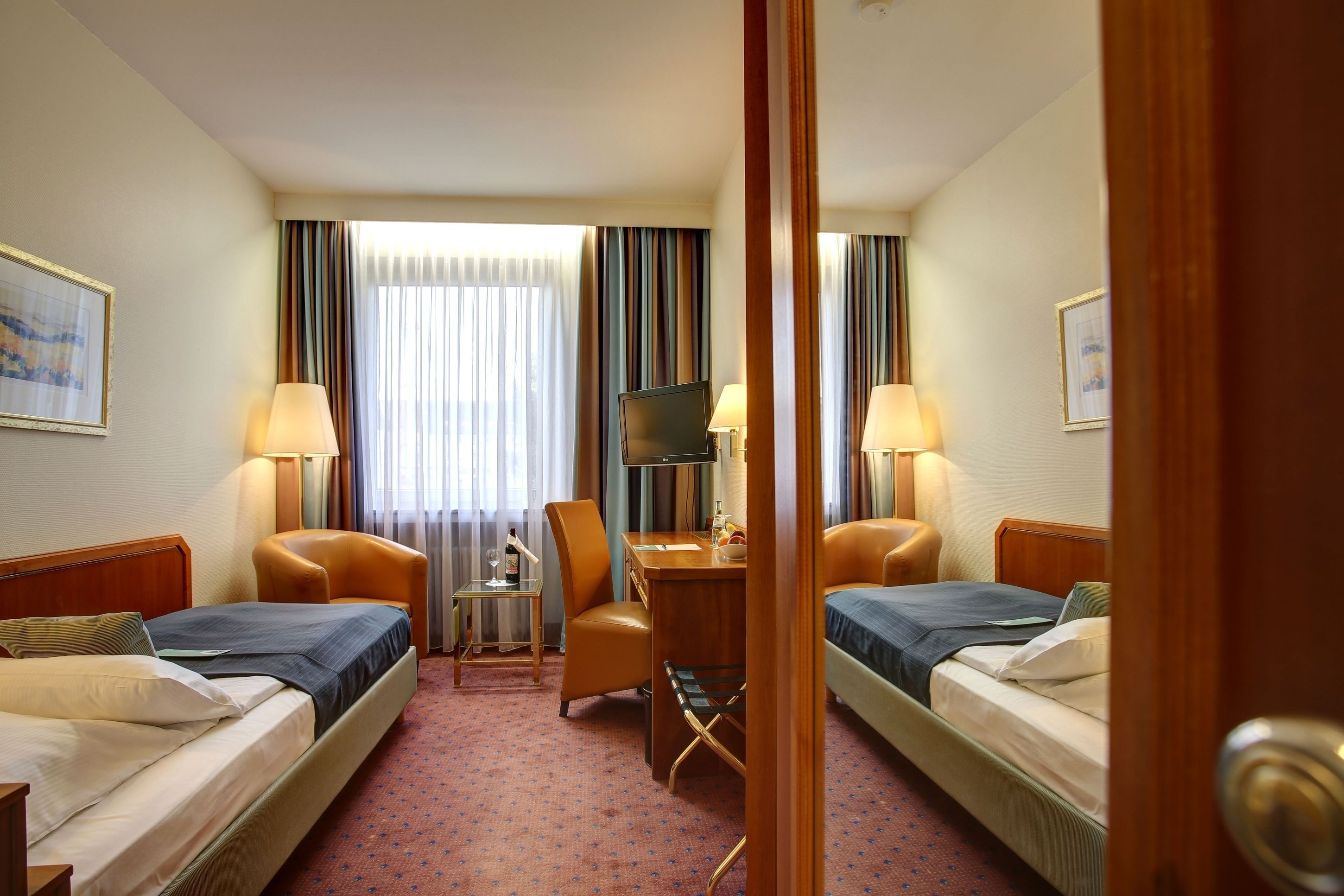 Quarto de hotel com duas camas, uma escrivaninha, uma cadeira, uma televisão e uma janela com cortinas.