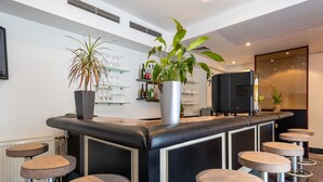 Uma área de bar com balcão preto, vários bancos e plantas em vasos.
