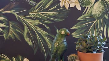 Um carro verde numa prateleira, rodeado por plantas e uma estatueta de papagaio.