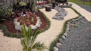 Um jardim bem cuidado com muro de pedra, palmeiras e um caminho de cascalho que leva a uma casa.