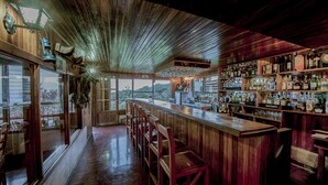 Um balcão com banquetas de madeira e prateleiras repletas de garrafas.