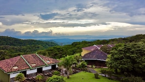 Um hotel com telhados em terracota, rodeado por vegetação exuberante e montanhas ao fundo.