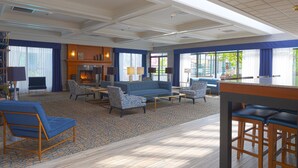 Um hall de hotel espaçoso com um sofá azul, poltronas, uma mesa de centro e uma lareira.