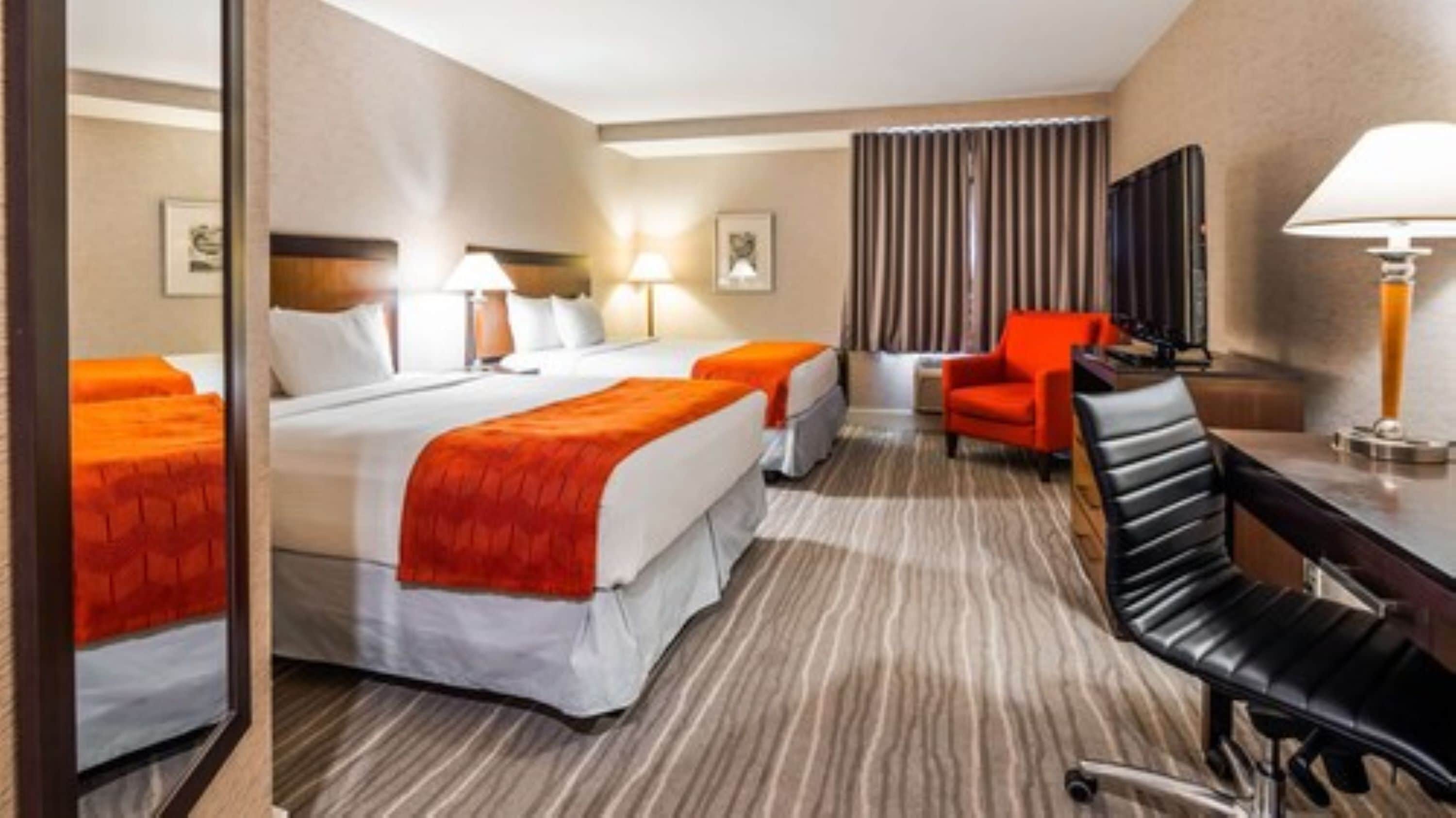 Quarto de hotel com duas camas, uma escrivaninha, uma cadeira, uma televisão e uma luminária.