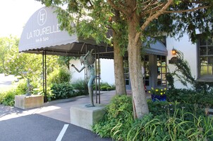 Entrada de hotel com uma placa indicando 'LA TOURELLE Inn & Spa', uma estátua e um edifício com acesso coberto.