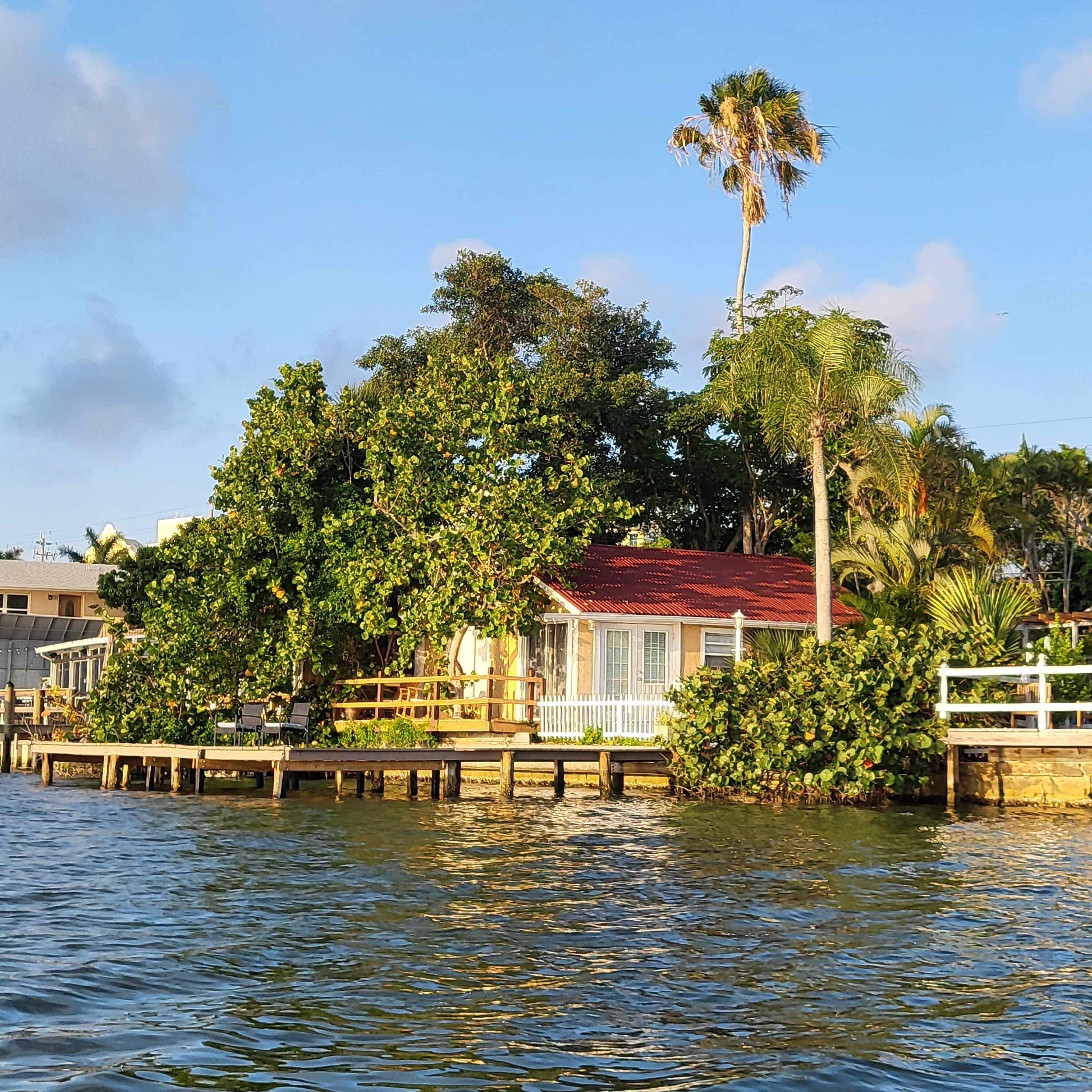 Um imóvel à beira-mar com um cais, uma casa com telhado vermelho e vegetação exuberante.