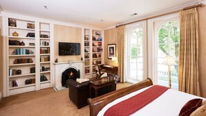 Quarto com uma cama grande, lareira, estantes de livros e vista para o verde pela janela.