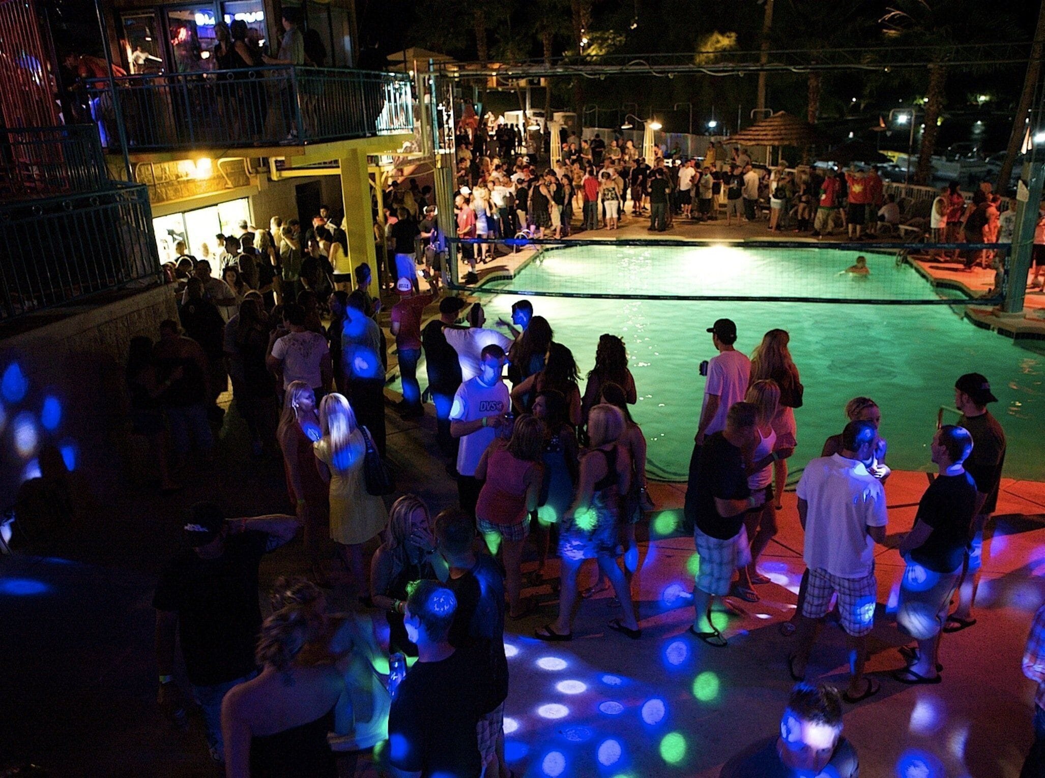Uma área de piscina ao ar livre movimentada à noite, com pessoas reunidas ao redor.