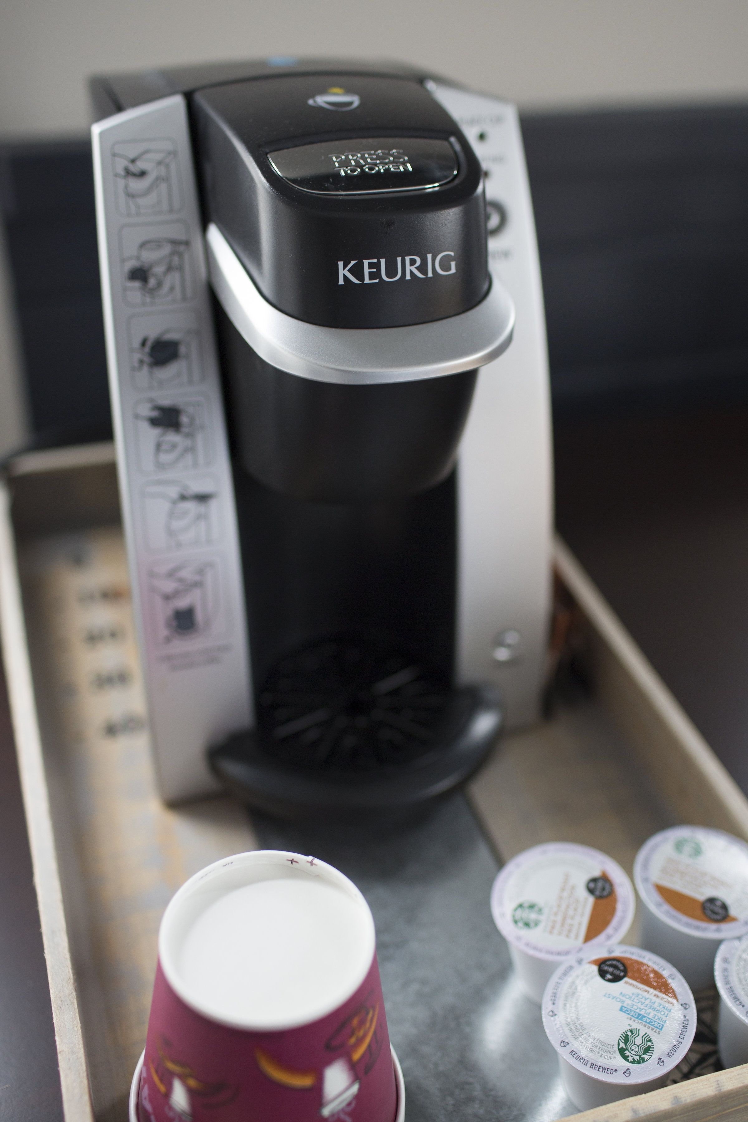 Máquina de café Keurig em um suporte com uma xícara descartável e sachês de café.