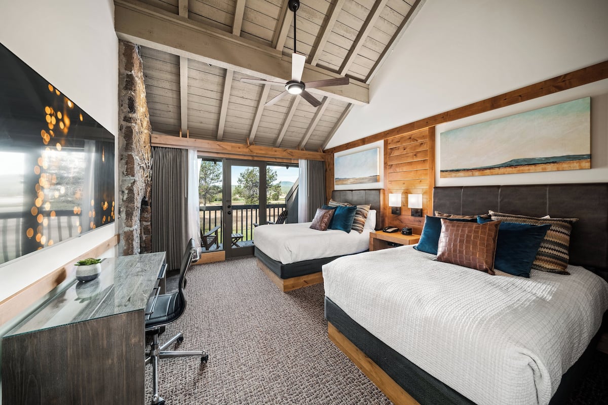 Quarto com duas camas, uma escrivaninha e varanda com vista.