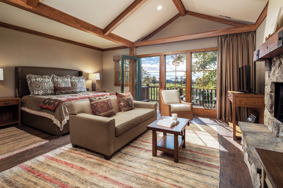Quarto com cama, sofá, mesa de centro, lareira e varanda com vista.