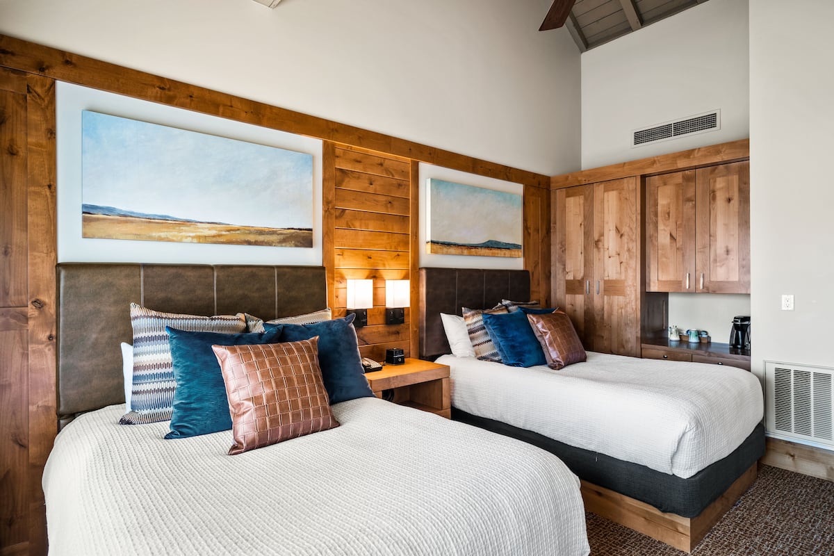 Quarto de hotel com duas camas, cabeceiras de madeira e grandes pinturas de paisagens.