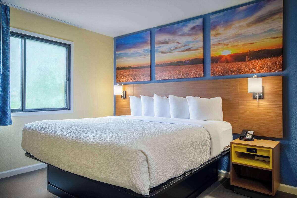 Quarto de hotel com uma cama grande, uma mesa de cabeceira e um telefone fixado na parede.