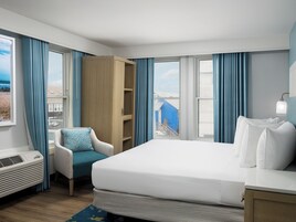 Quarto de hotel com cama, poltrona, escrivaninha, guarda-roupa e vista para a praia.