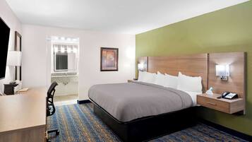 Quarto de hotel com cama, mesa de cabeceira, abajur e vista para um banheiro.