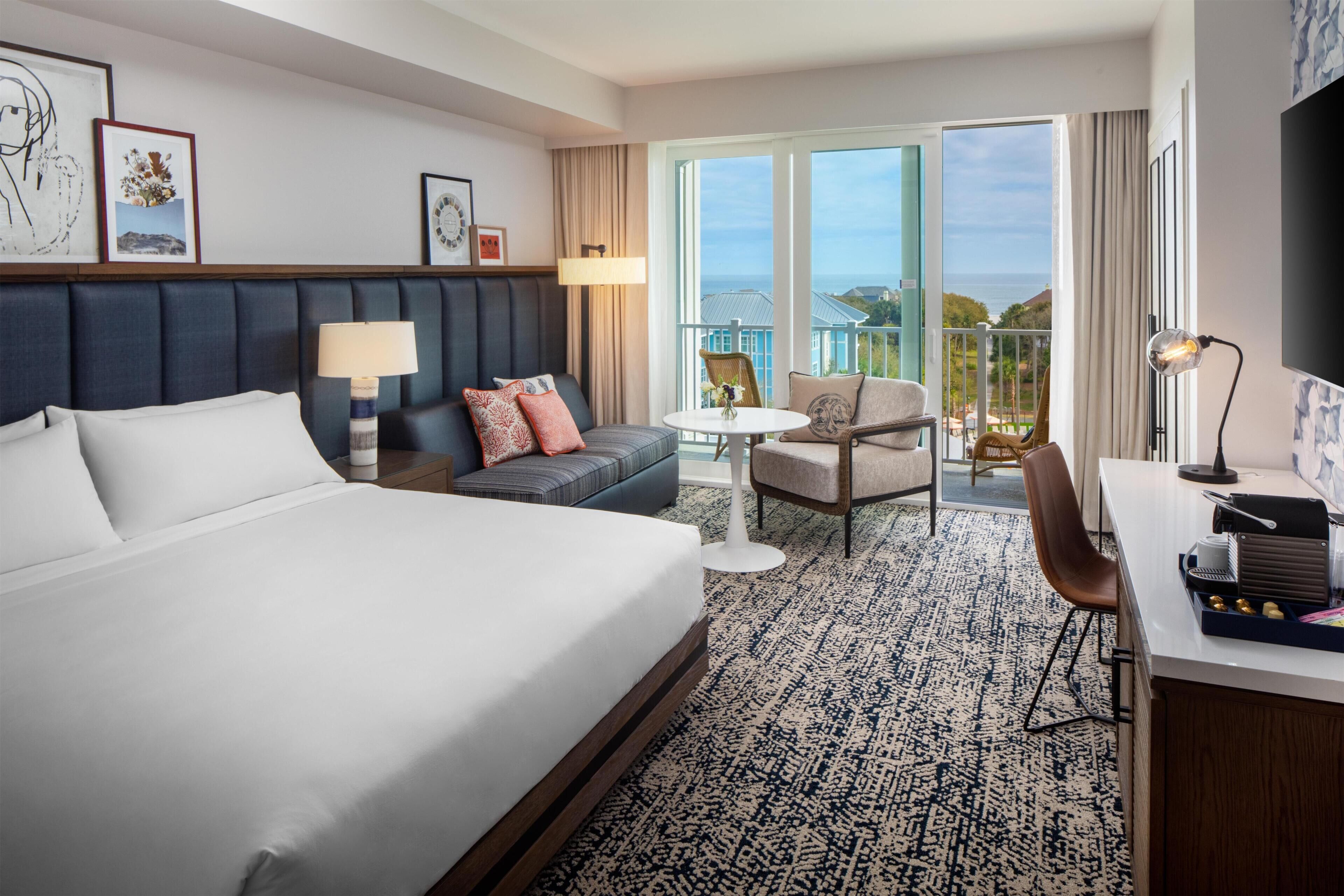 Quarto de hotel com cama, sofá, mesa pequena, cadeira e varanda com vista.