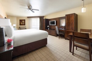 Quarto de hotel com uma cama grande, uma escrivaninha com um computador, uma televisão e um ventilador de teto.