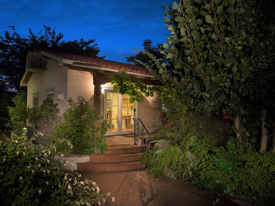 Uma casa com telhado de telhas, entrada frontal com degraus e jardim com diversas plantas.