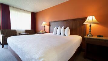 Quarto de hotel com uma cama grande, duas mesas de cabeceira, uma cadeira e um abajur.
