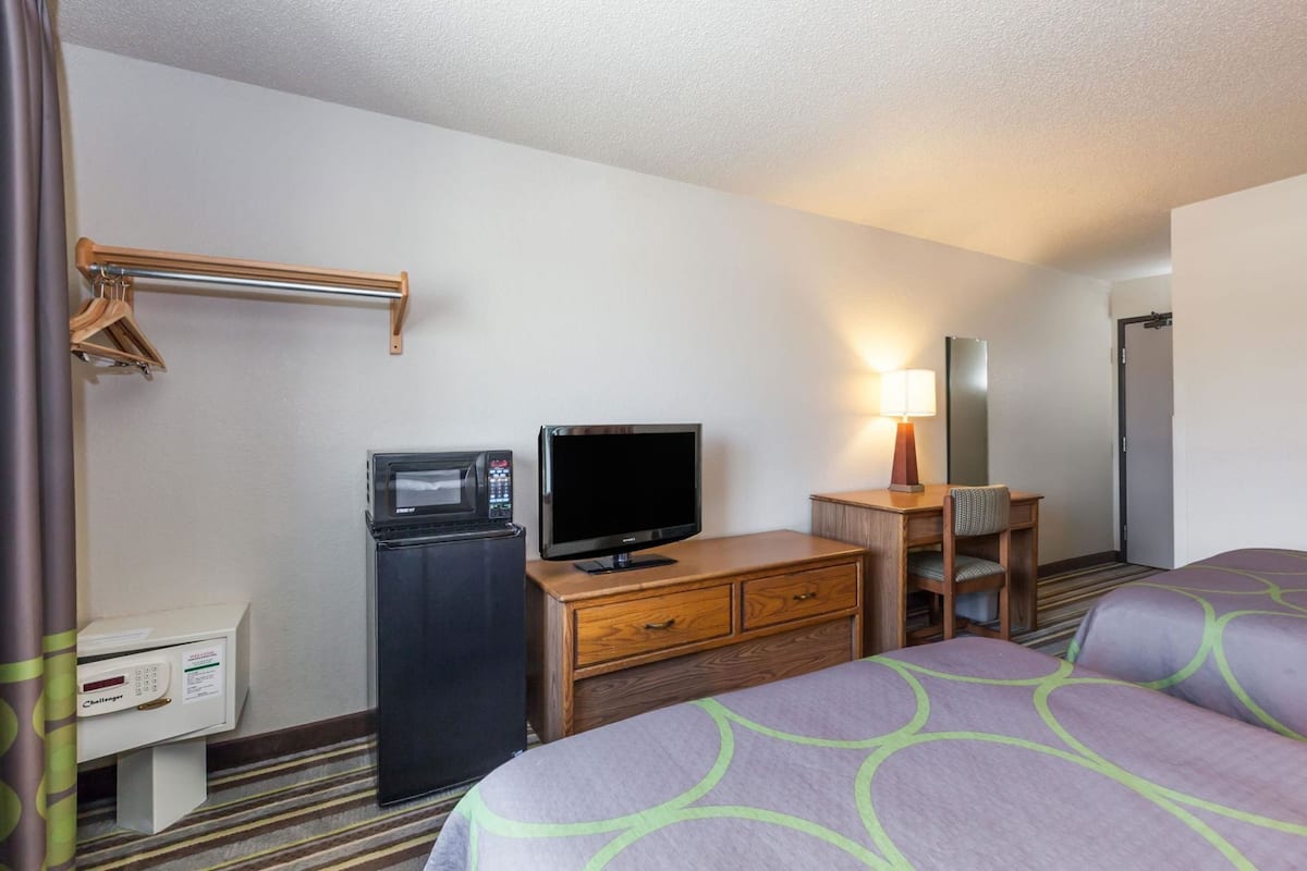Quarto de hotel com cama, escrivaninha, televisão, micro-ondas, minibar e luminária.