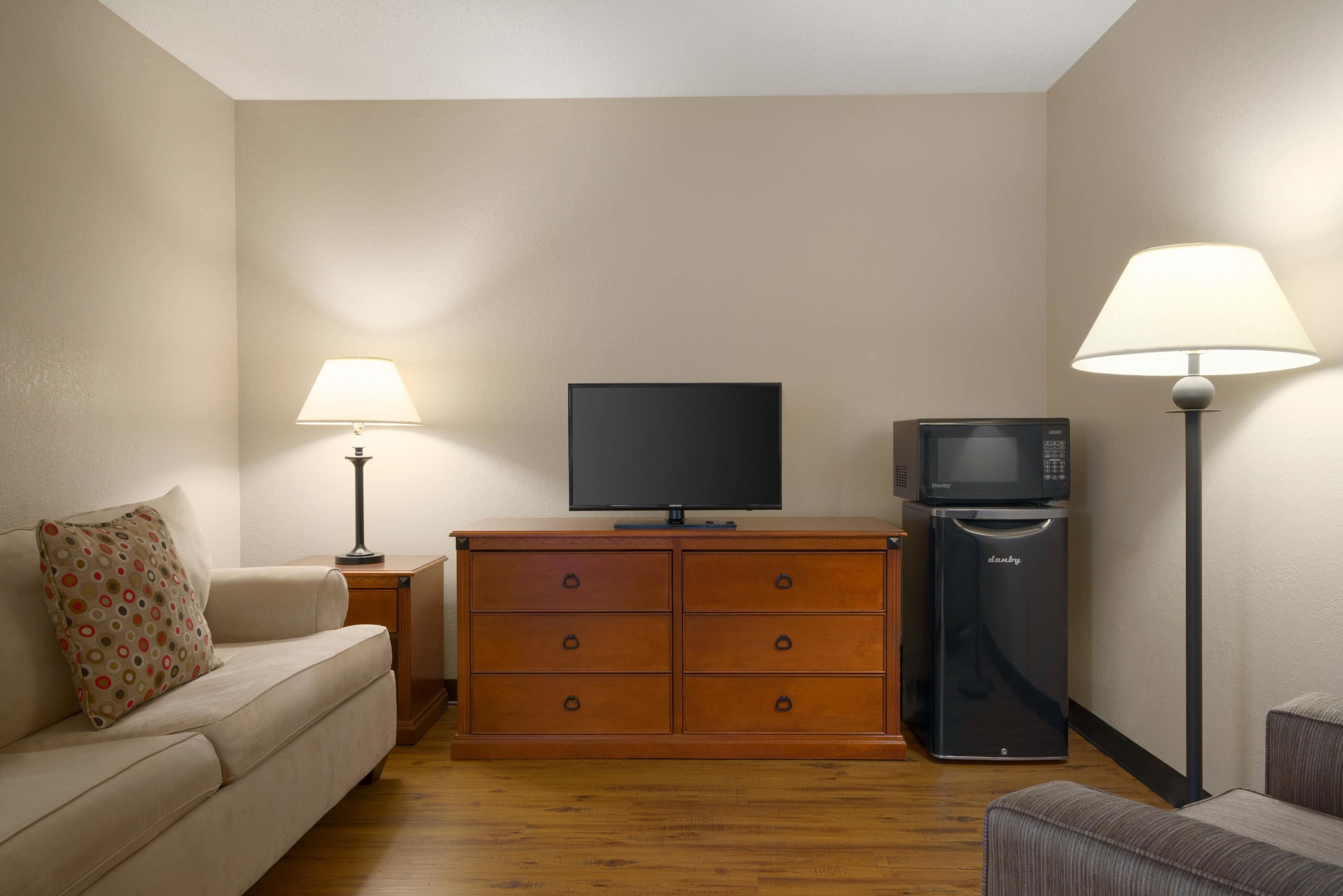 Quarto de hotel com cómoda de madeira, televisão de tela plana, micro-ondas, luminária e sofá.