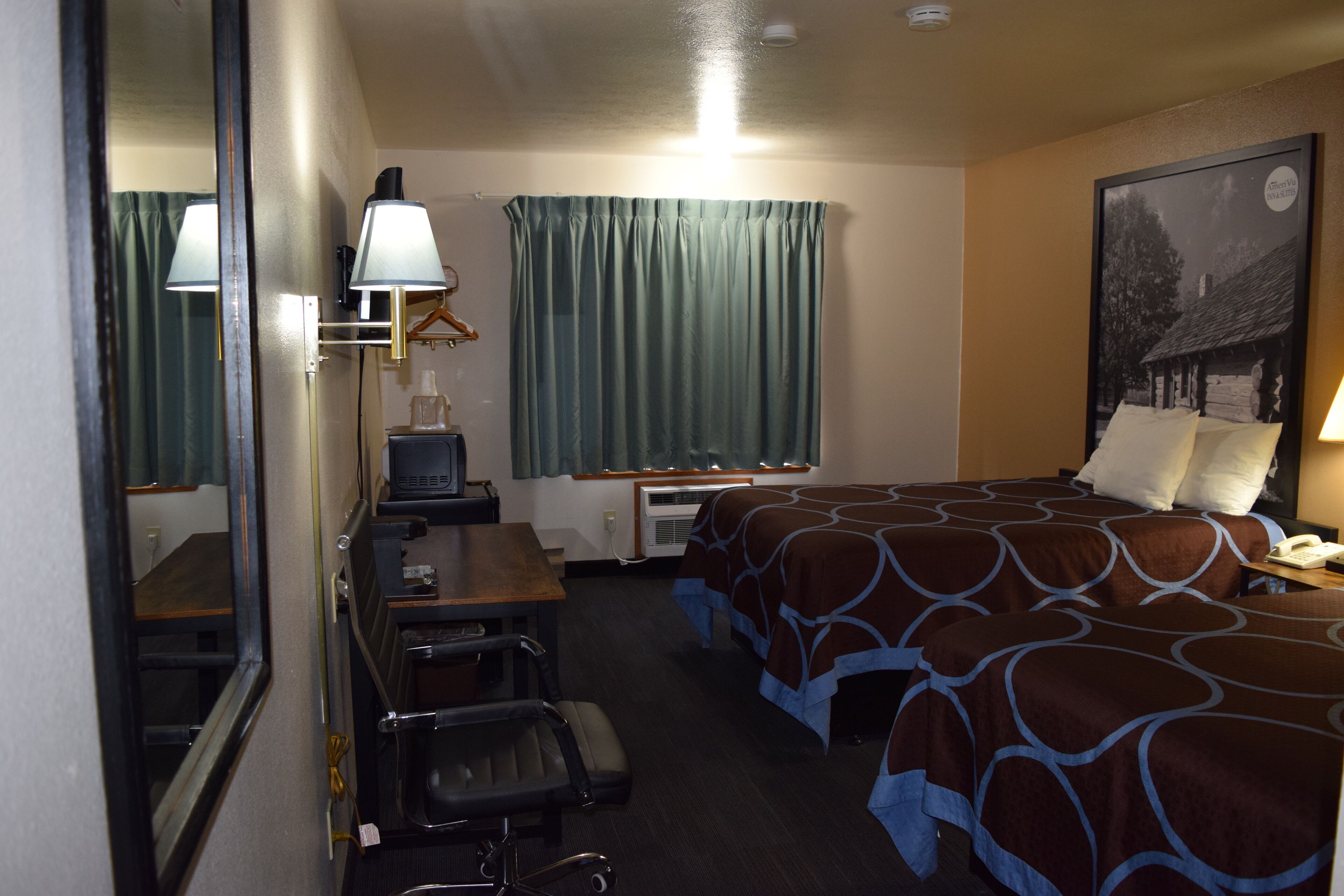 Quarto de hotel com cama, escrivaninha, cadeira e um espelho grande.
