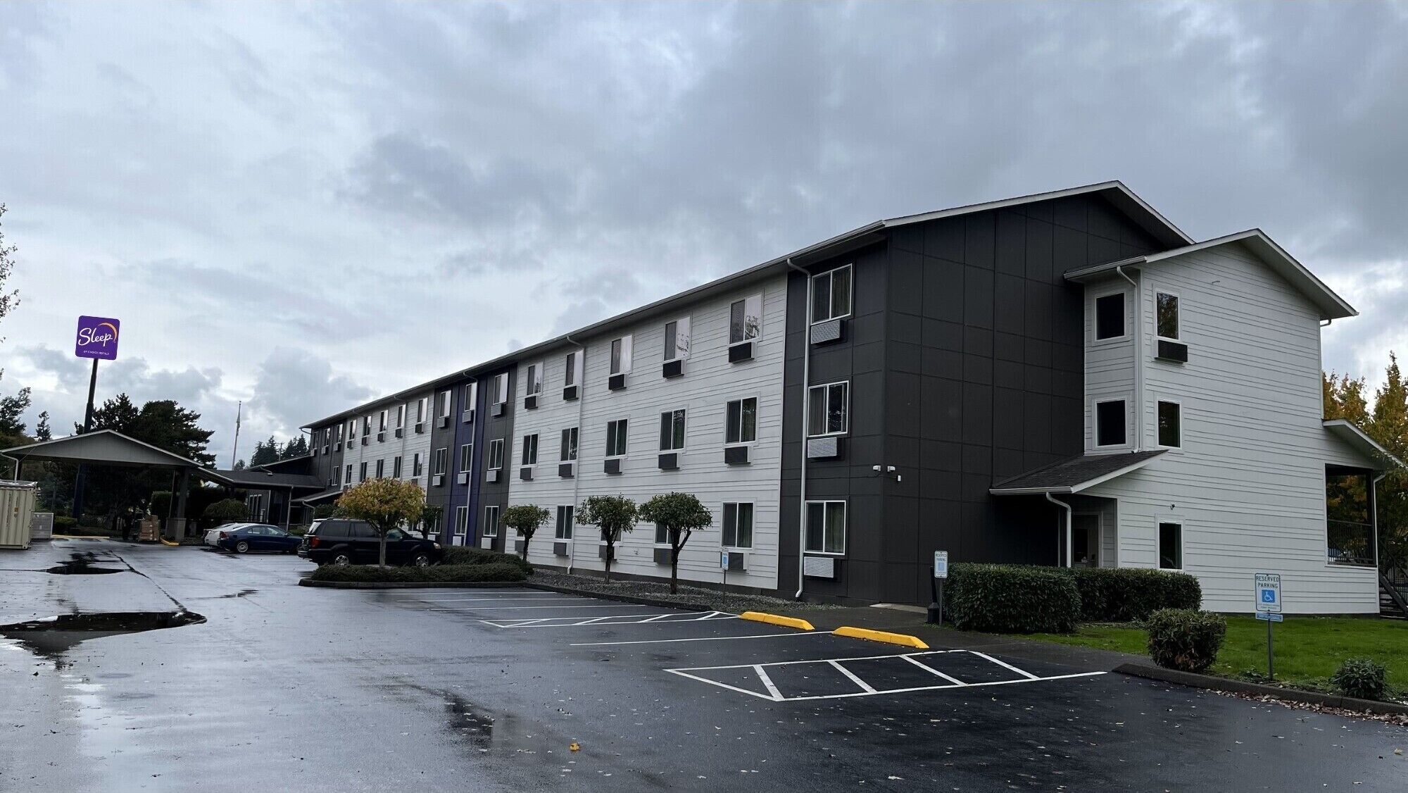 Hotel com vários andares, estacionamento, entrada coberta e placa indicando vagas reservadas.