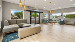 Um hall moderno com sofá, um banquinho e cadeiras, uma mesa redonda e grandes janelas com vista para o exterior.