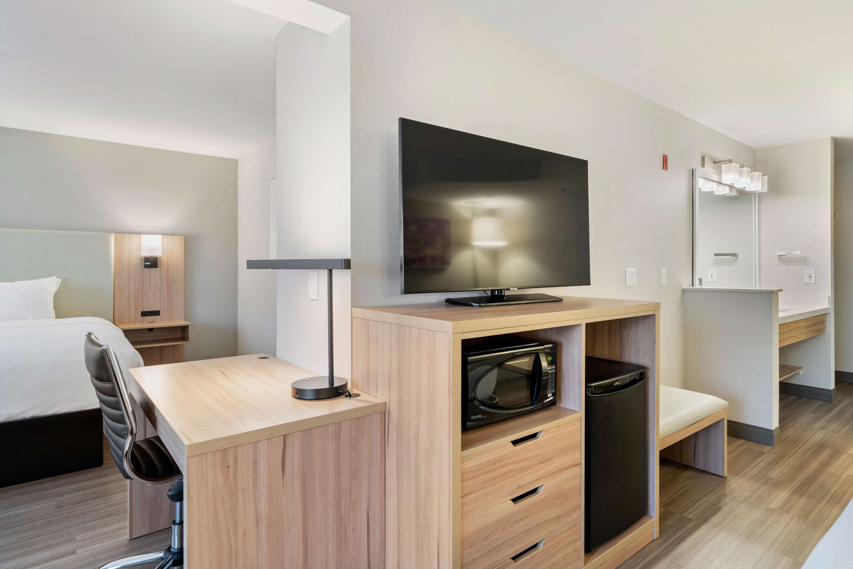 Quarto de hotel moderno com uma cama, uma escrivaninha com televisão de tela plana, micro-ondas e um pequeno frigorífico.