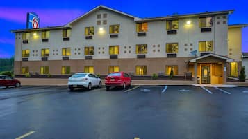 Um motel com estacionamento, vários carros estacionados e uma placa indicando o nome do motel.