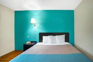 Quarto de hotel com parede de destaque azul-turquesa, cama com roupa de cama branca, mesa de cabeceira com abajur e telefone.
